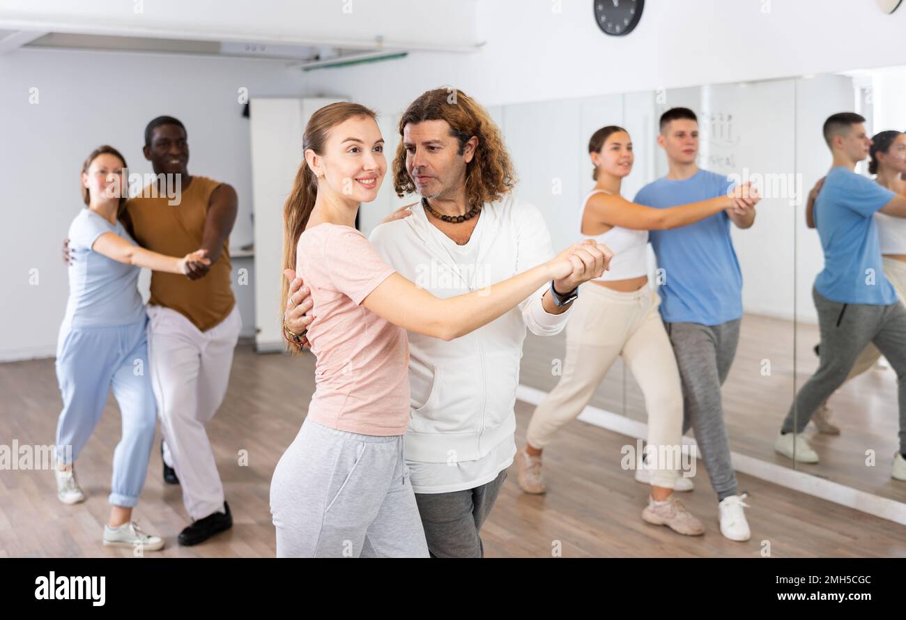 Smiling multiracial men and women enjoying partner dance while training ...