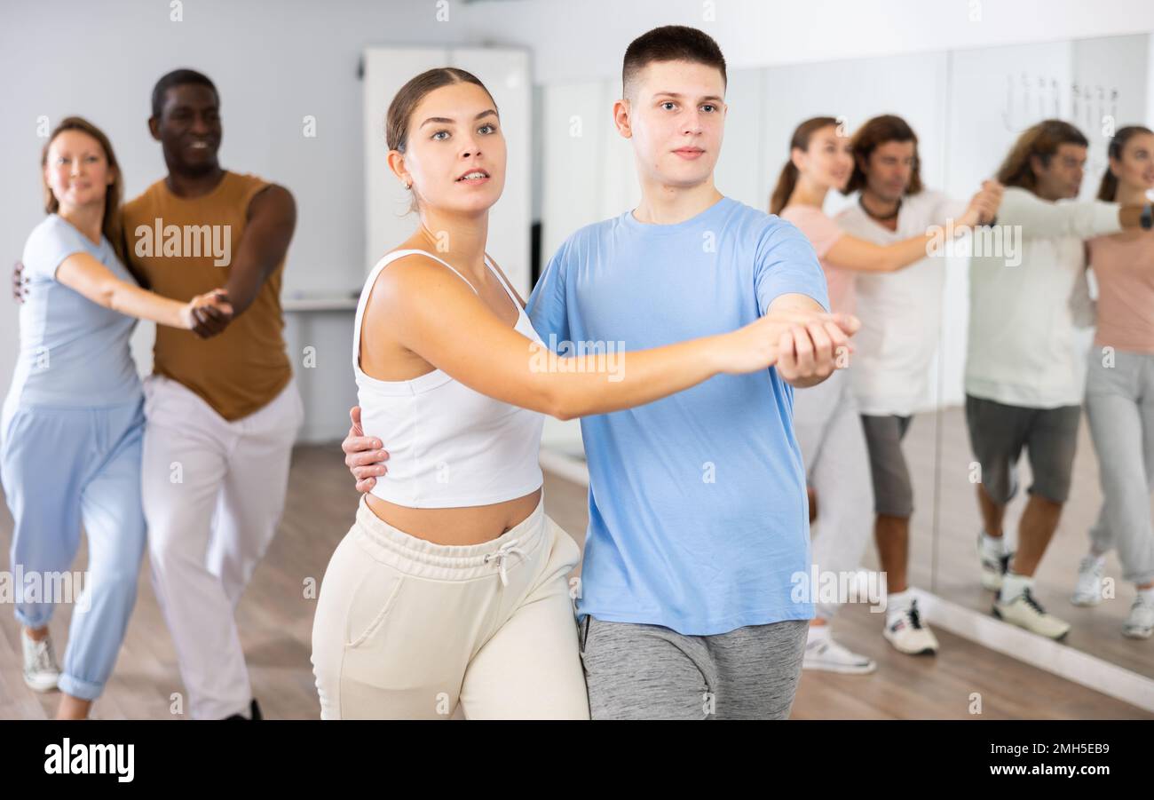 Group of diverse happy adult people dancing modern social dances in pairs at fitness studio ...