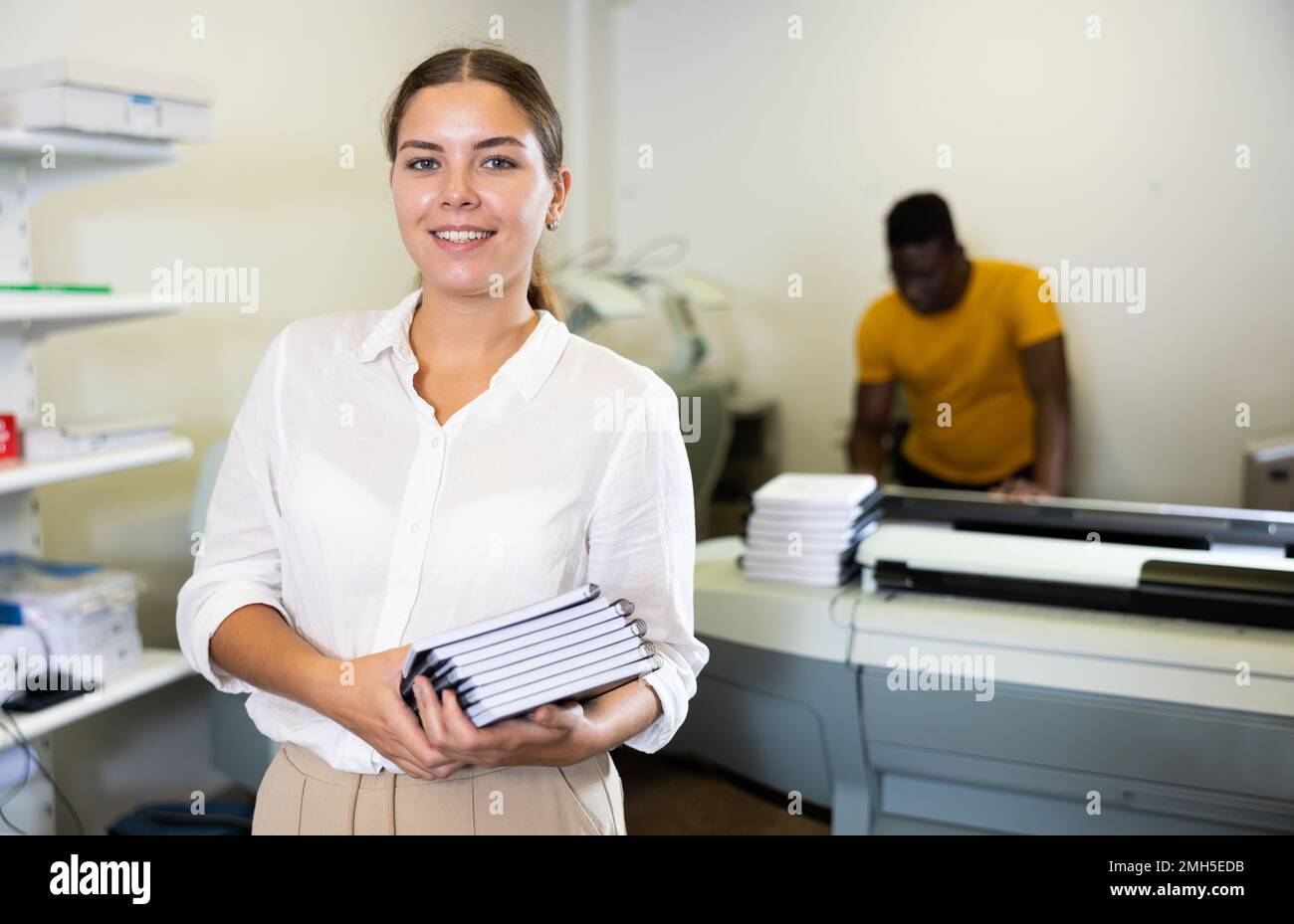 Portrait of friendly female employee of printing house with stack of ...