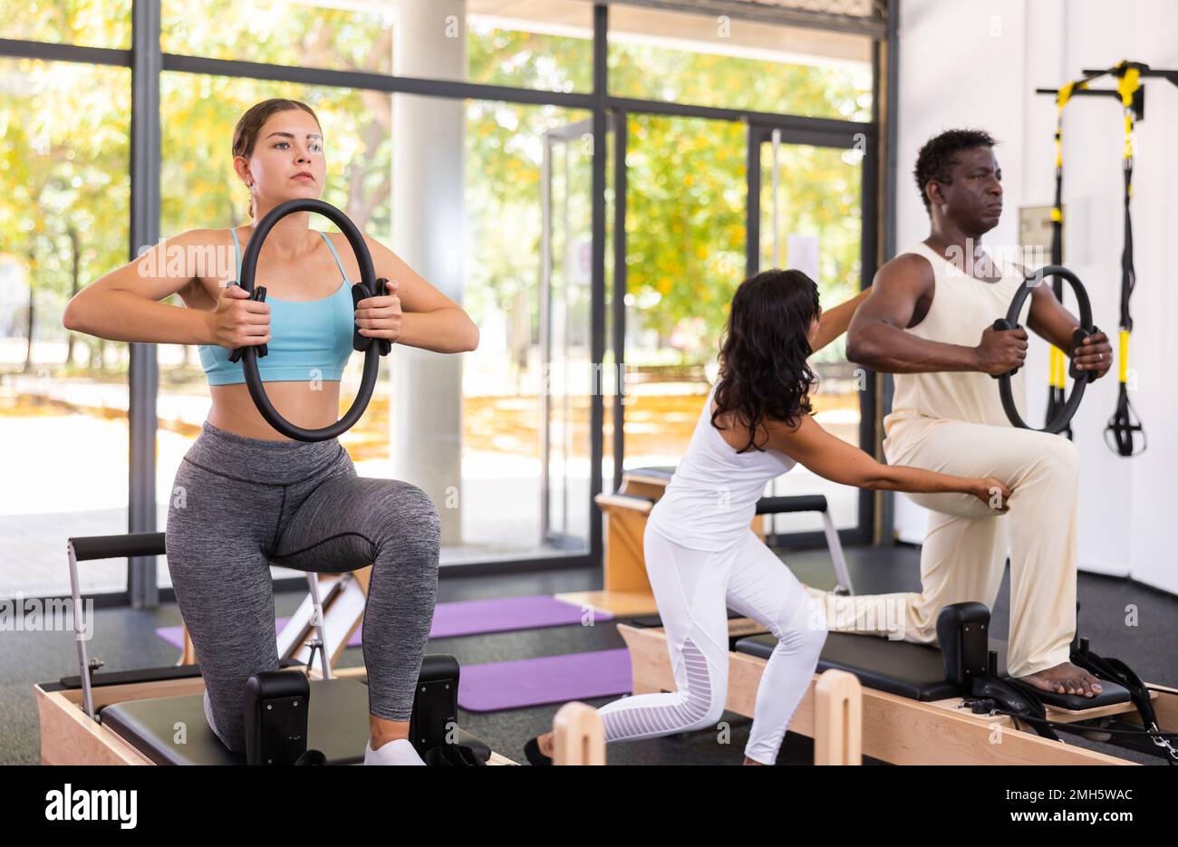 Latin female instructor helping African American man with ring in gym ...