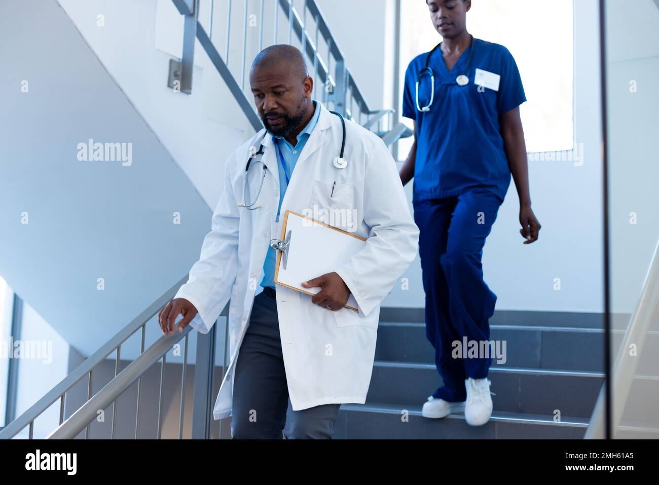 African american female and male doctor walking down hospital staircase ...