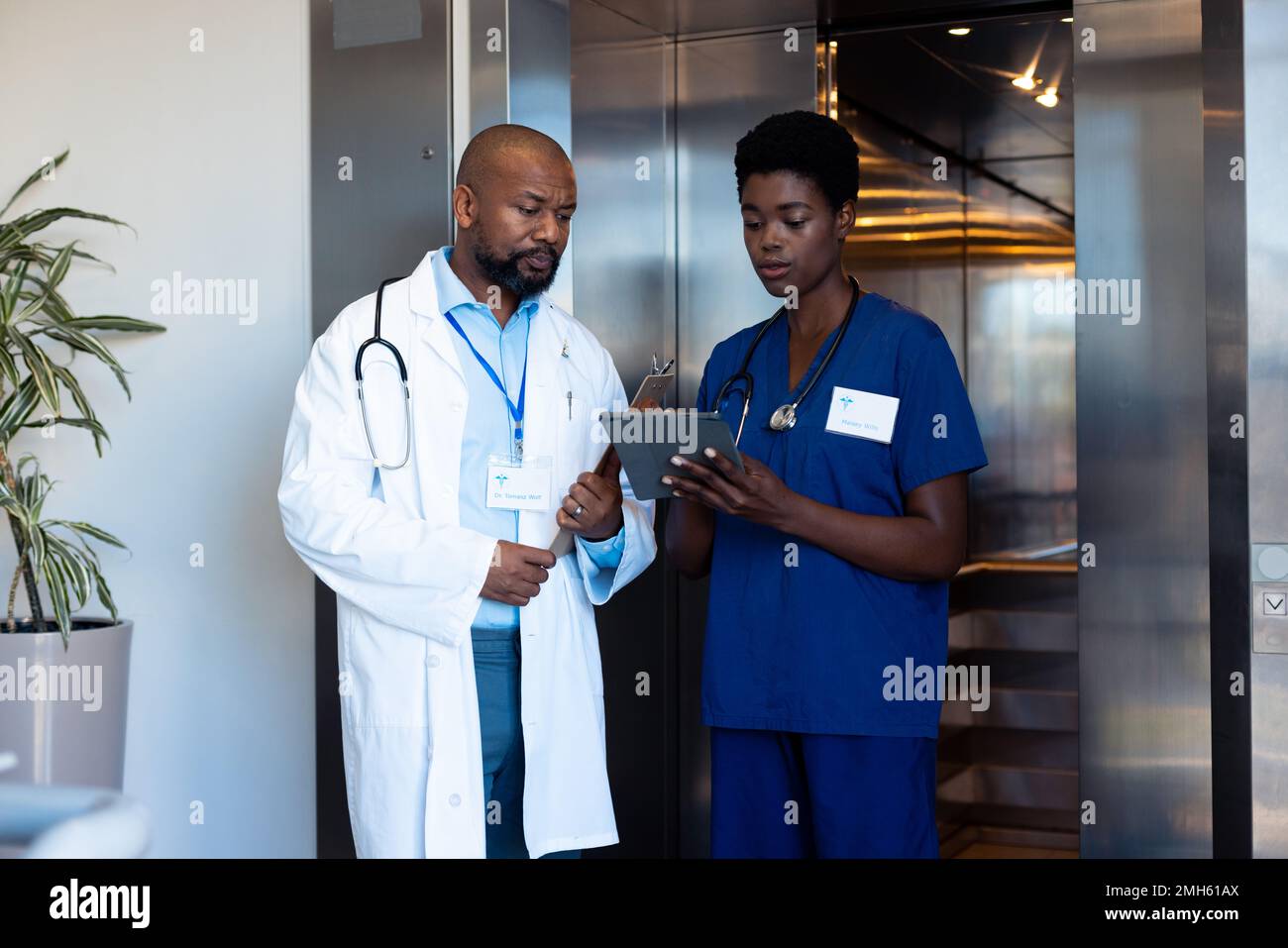 African american female and male doctor looking at tablet by lift in ...
