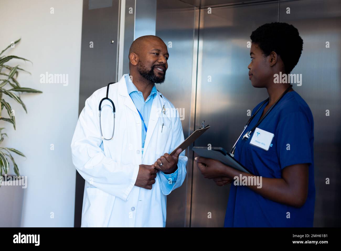 Happy african american female and male doctor talking by lift in ...