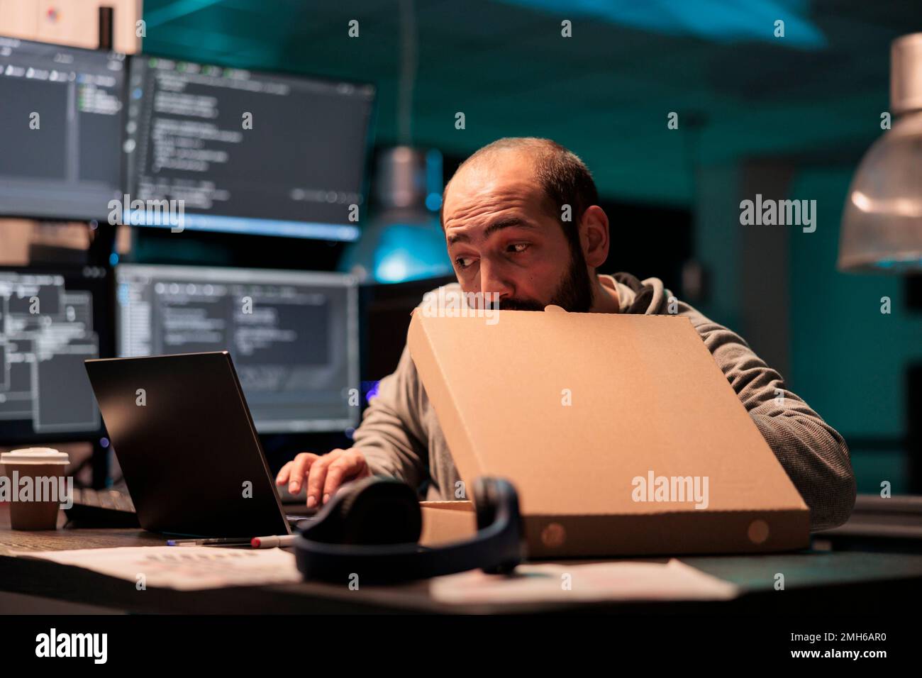 Software developer eating pizza from takeaway delivery, taking bite of ...
