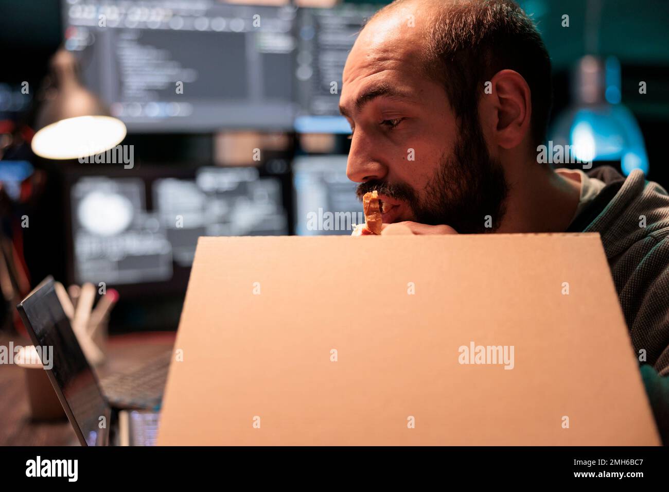 Database coder eating pizza from takeaway delivery, taking bite of food ...