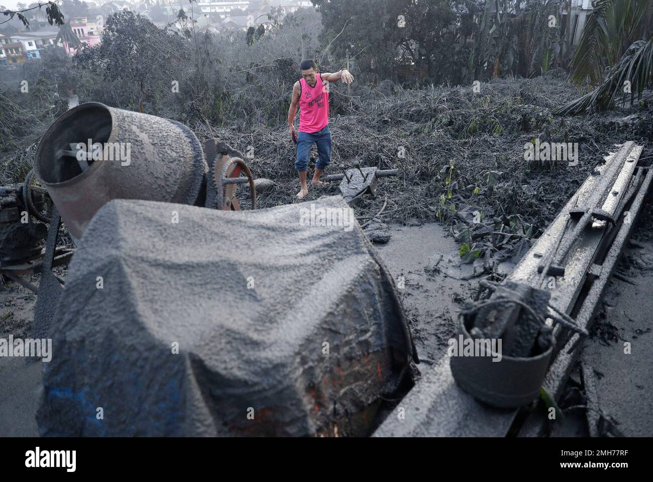 A man walks along ash fall covered plants and equipment as Taal Volcano ...