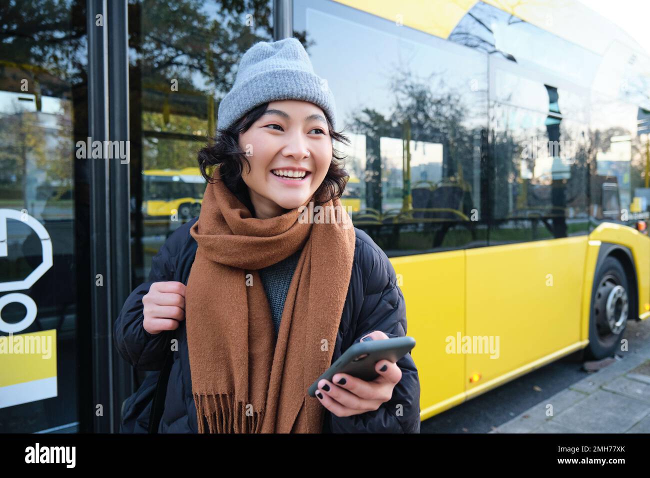 Portrait of girl standing near bus on a stop, waiting for her public transport, schecks schedule ...
