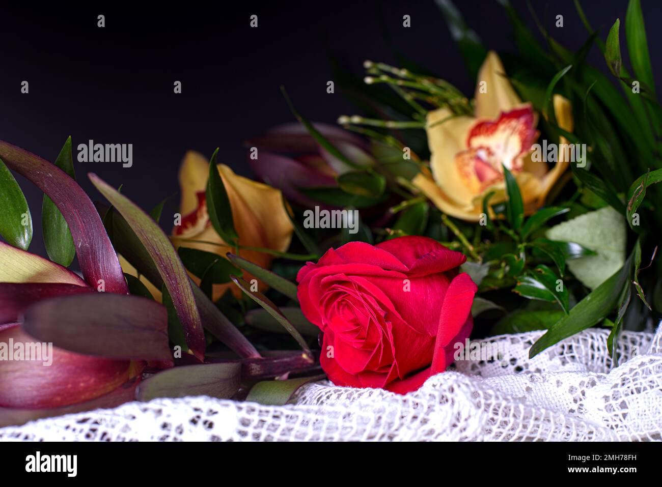 Close up bouquet with one red rose and orchids on handmade white lace ...