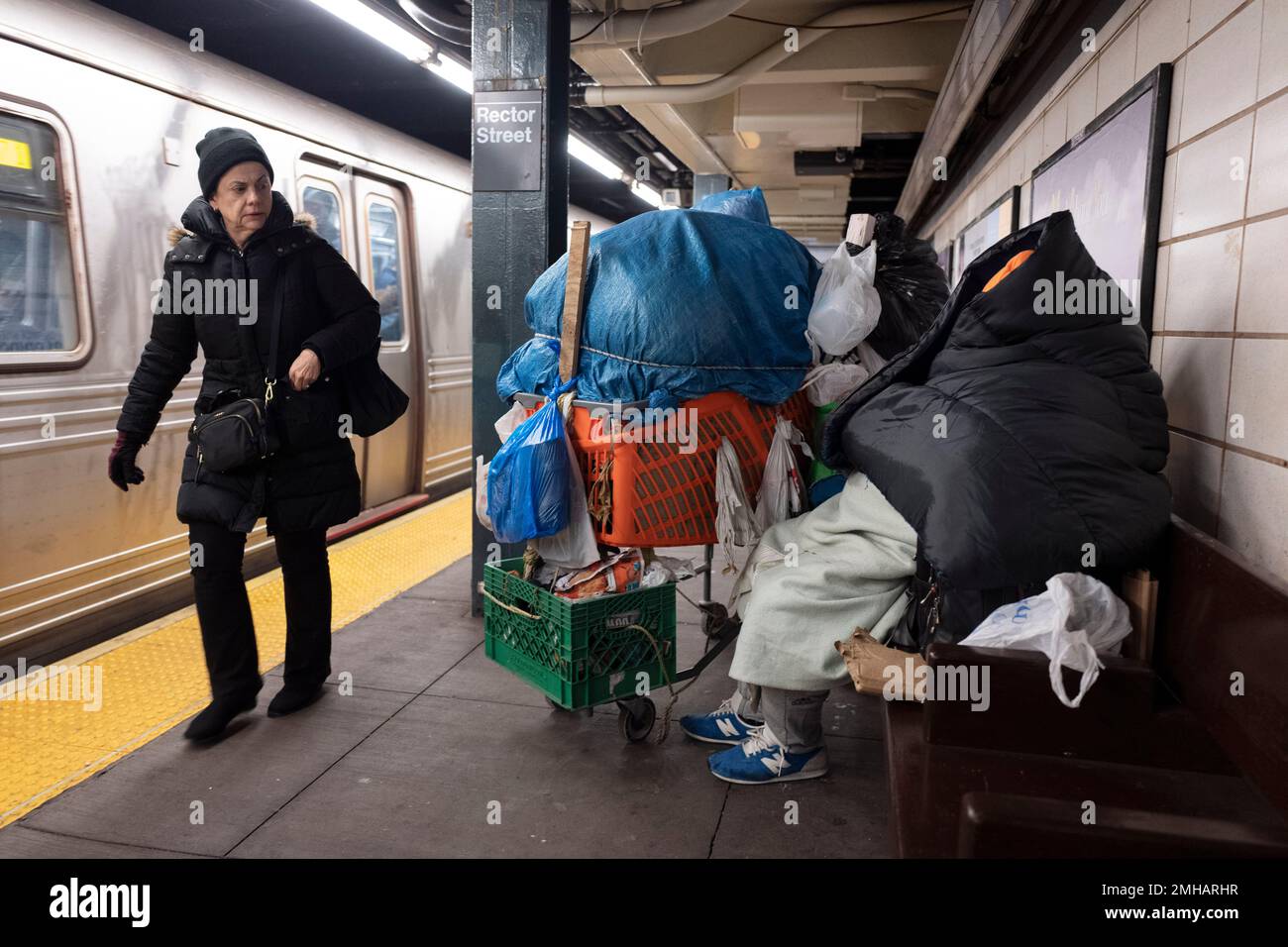 A woman walks past a homeless person sleeping on a subway station bench ...