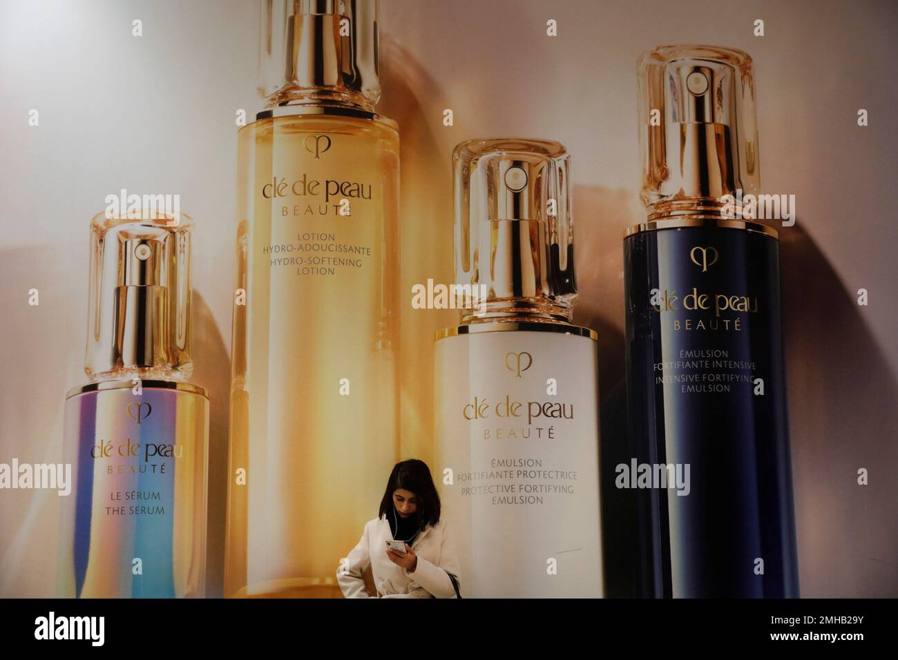 A woman is dwarfed by a large cosmetics advertisement as she looks at ...