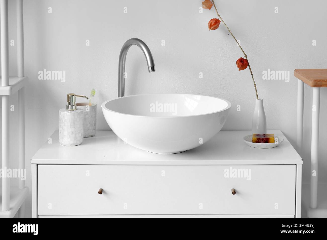 Ceramic sink, vase with plant branch and bath accessories on drawers in ...