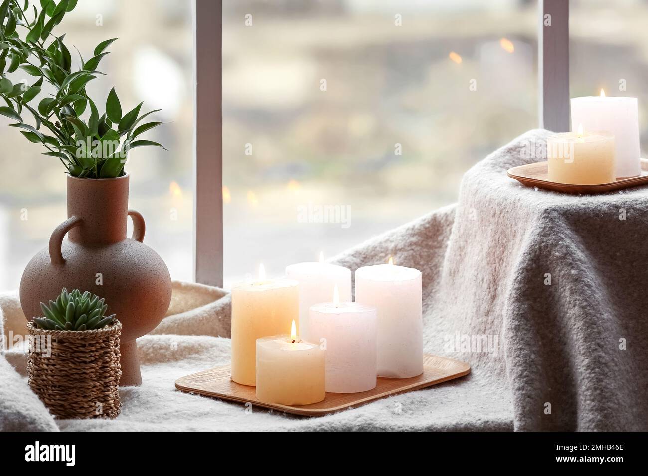 Woollen cover with burning candles and houseplants at windowsill Stock ...