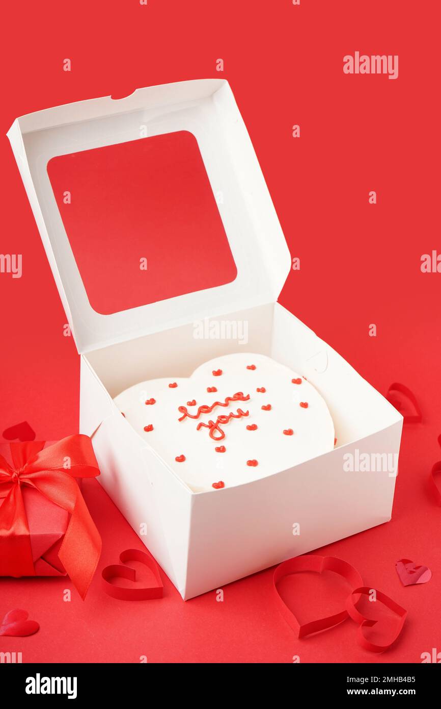 Opened box with tasty bento cake, gift and hearts on red background ...
