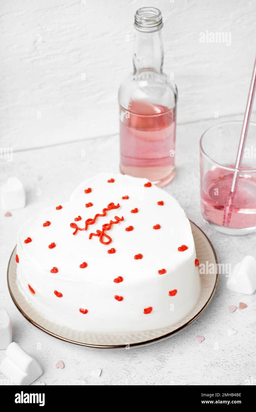 Plate with heart-shaped bento cake, bottle and glass of tasty drink on ...