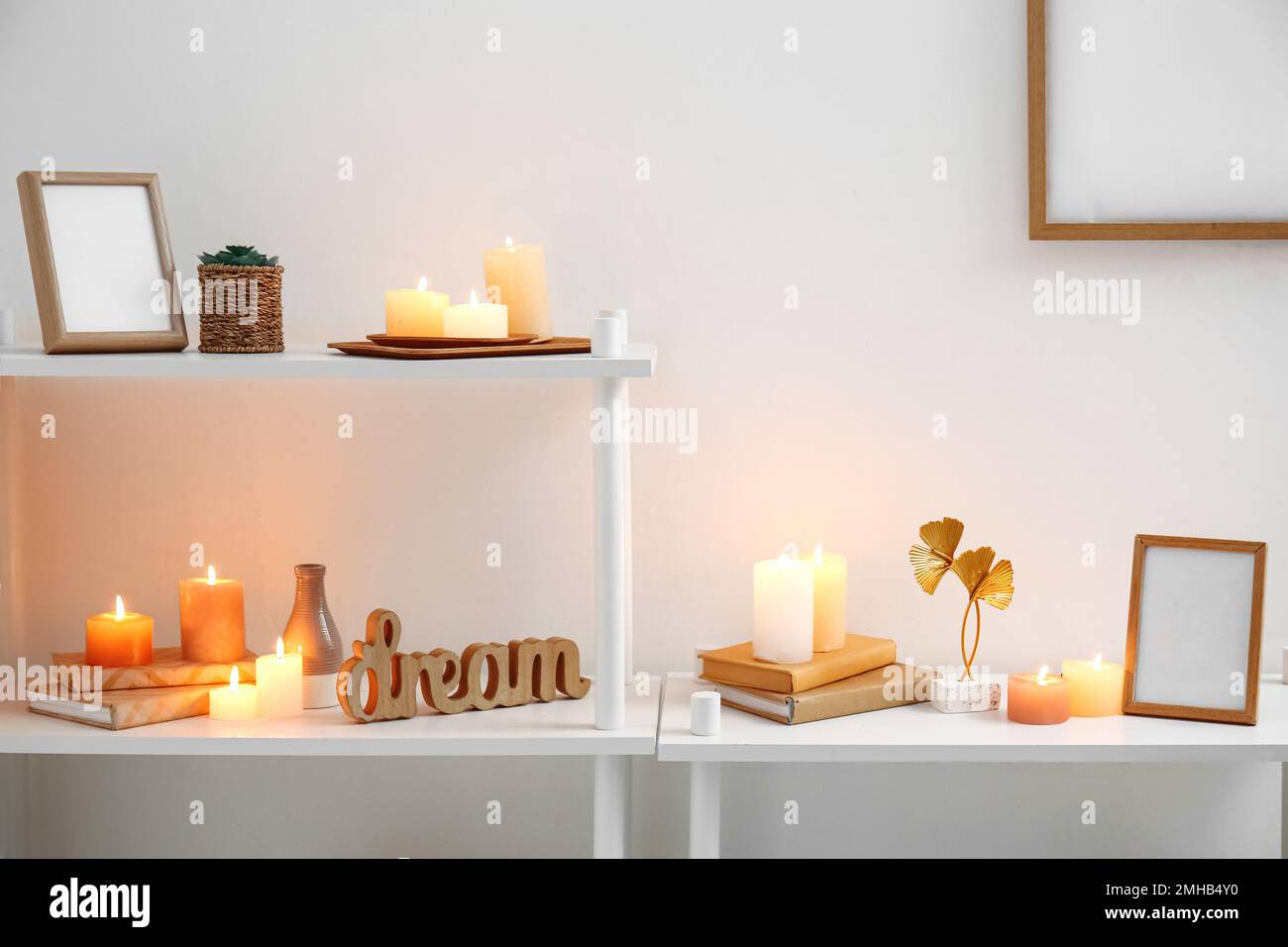 Shelving units with burning candles, books and frames near light wall ...