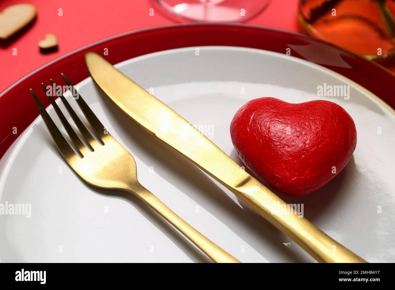 Plate with heart figure and golden cutlery on red background, closeup ...
