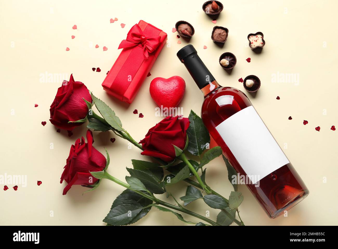 Bottle of wine, chocolate candies, rose flowers and gift on beige ...