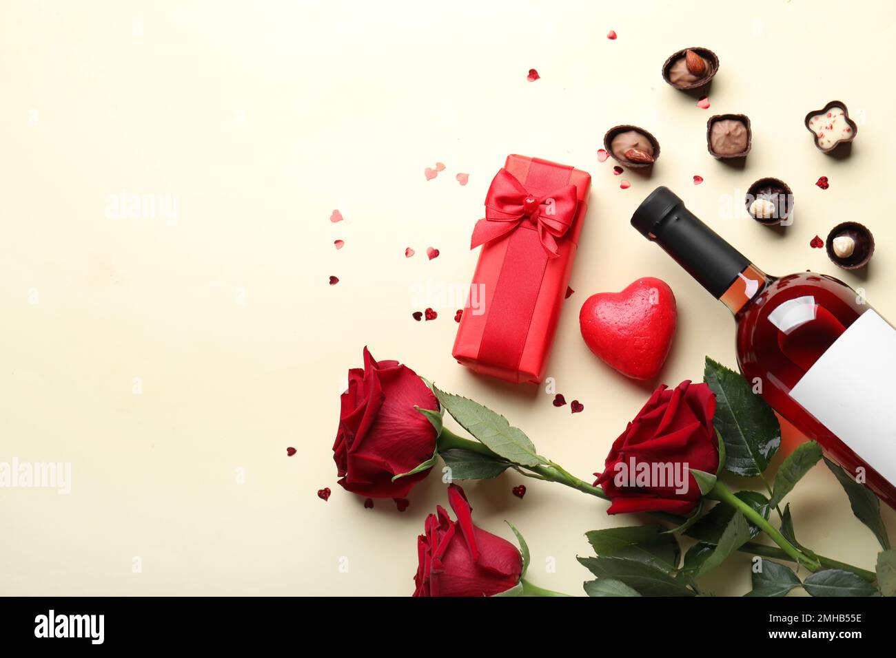 Bottle of wine, chocolate candies, rose flowers and gift on beige ...