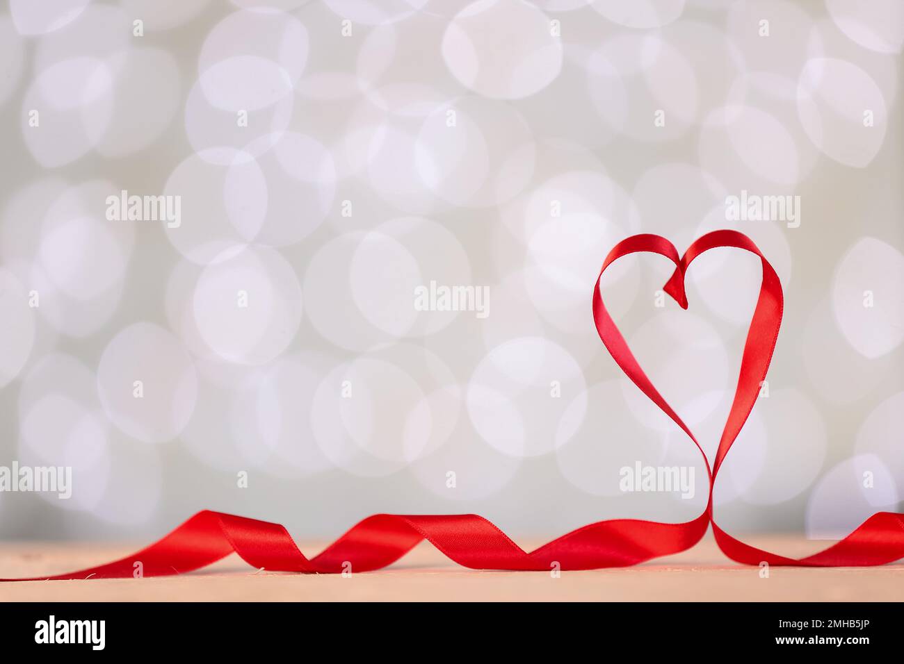 Heart made of red satin ribbon on table against blurred lights ...