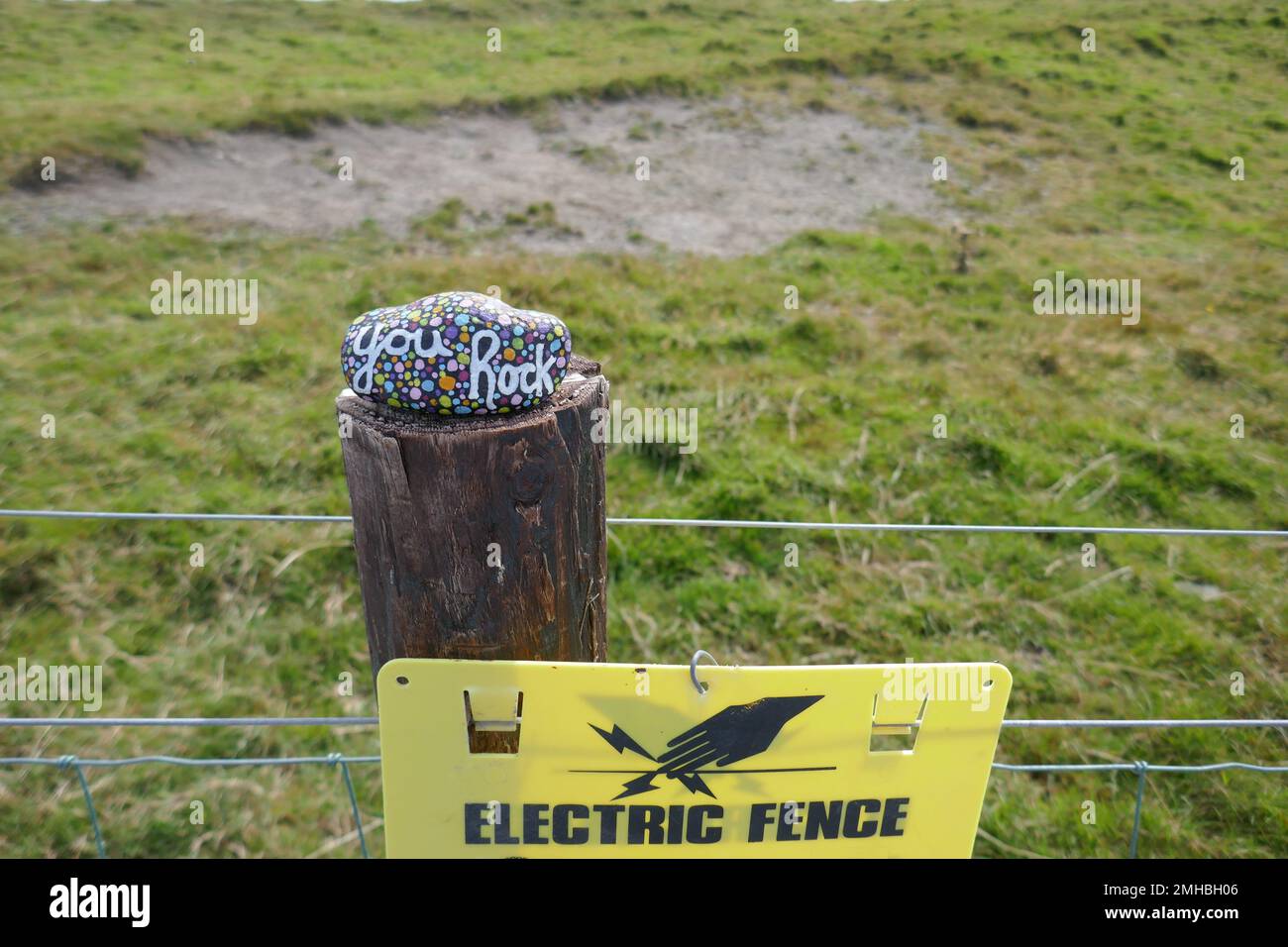 Electric fence with warning sign and kindness rock on wooden fence post ...