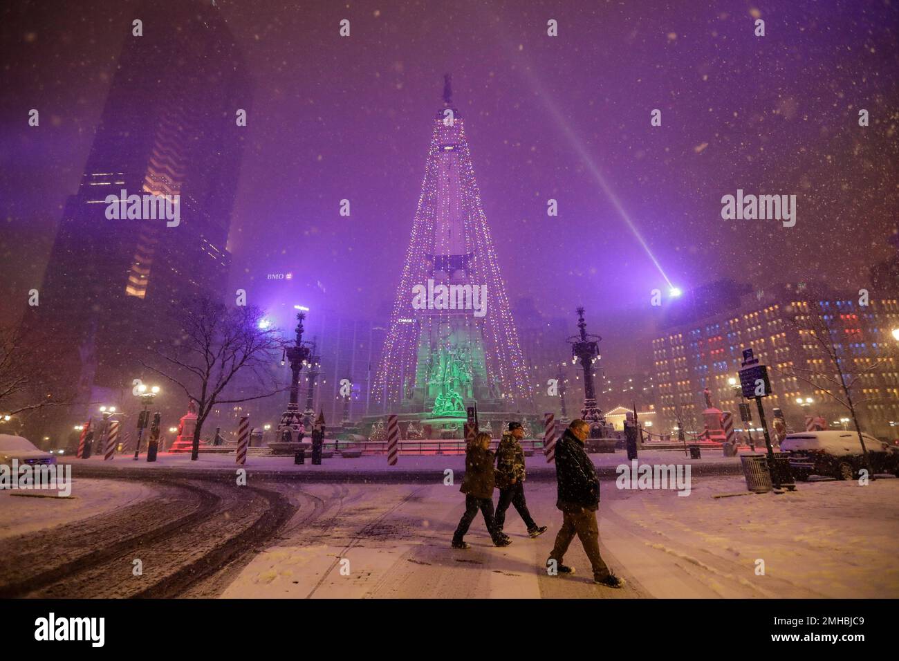 Pedestrians walk across an intersection as snow falls in downtown ...