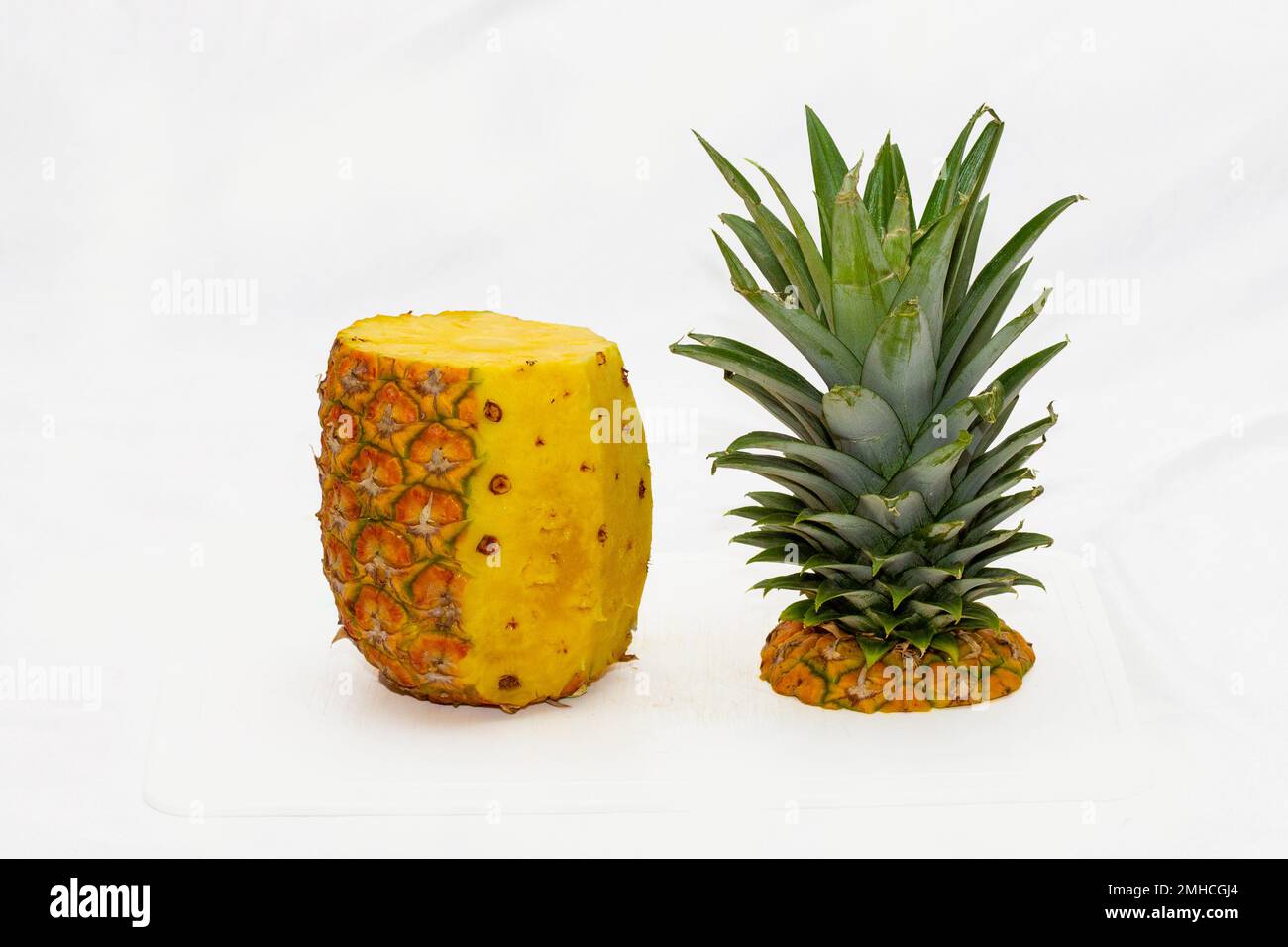 pineapple with half of the peel peeled and the crown removed on a white ...