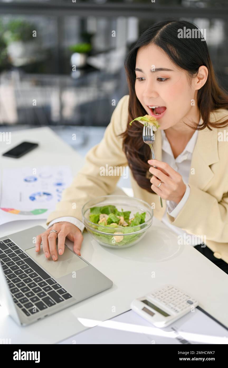 Portrait, Hungry and busy millennial Asian businesswoman eating salad ...