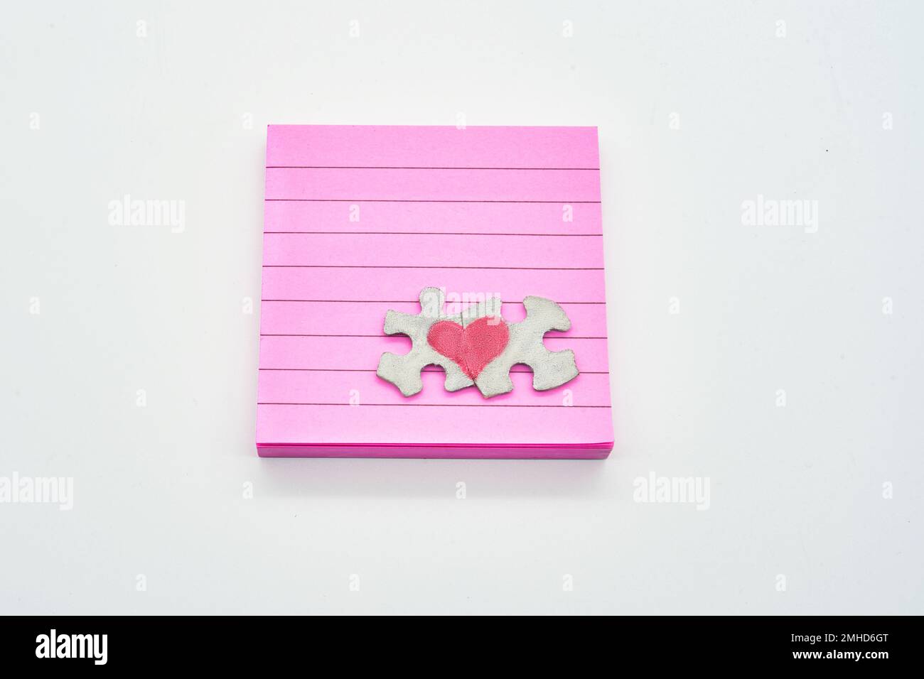 Heart on connected puzzle pieces on top of post it note pink note pad ...