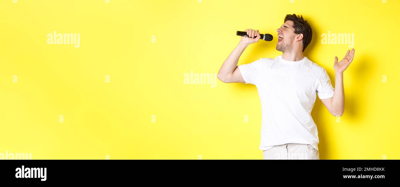 Young man singer holding microphone, reaching high note and singing ...