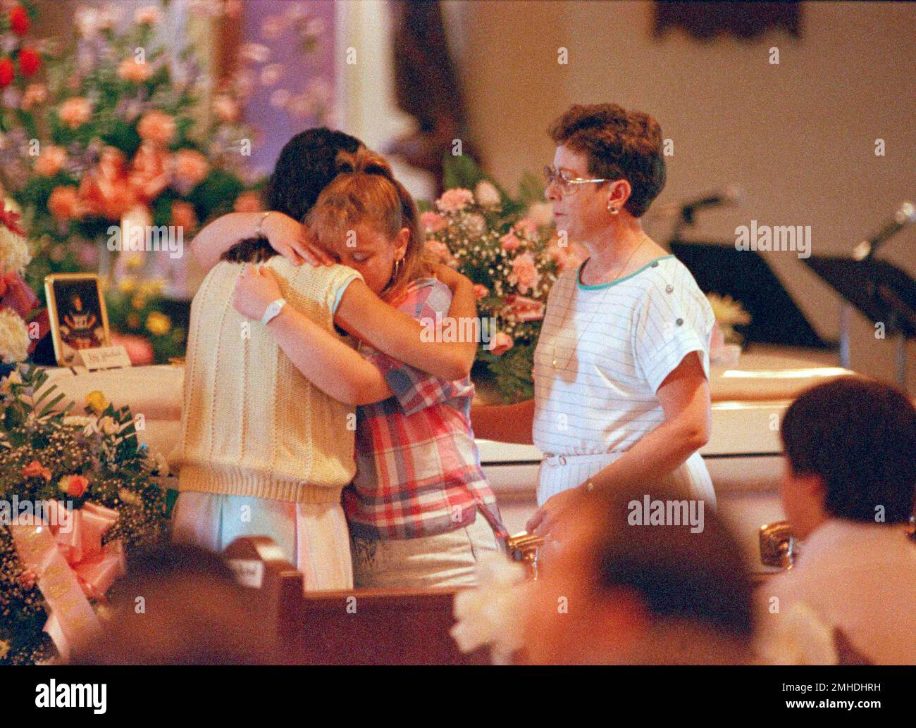 Two young women hold each other as they stand in front of the casket of ...