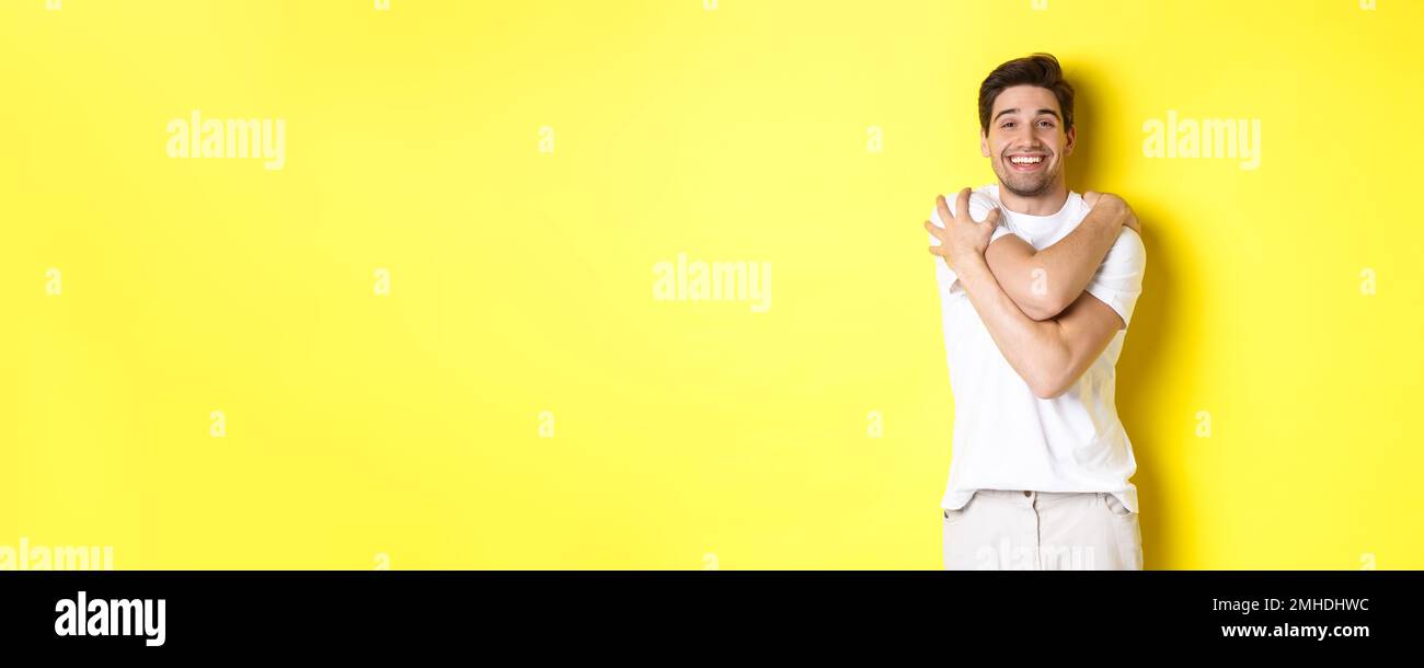 Happy kind guy hugging himself and smiling, standing pleased against ...