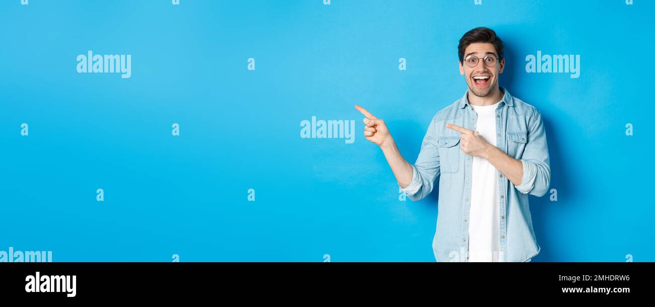 Excited handsome man in glasses pointing fingers left, looking happy ...