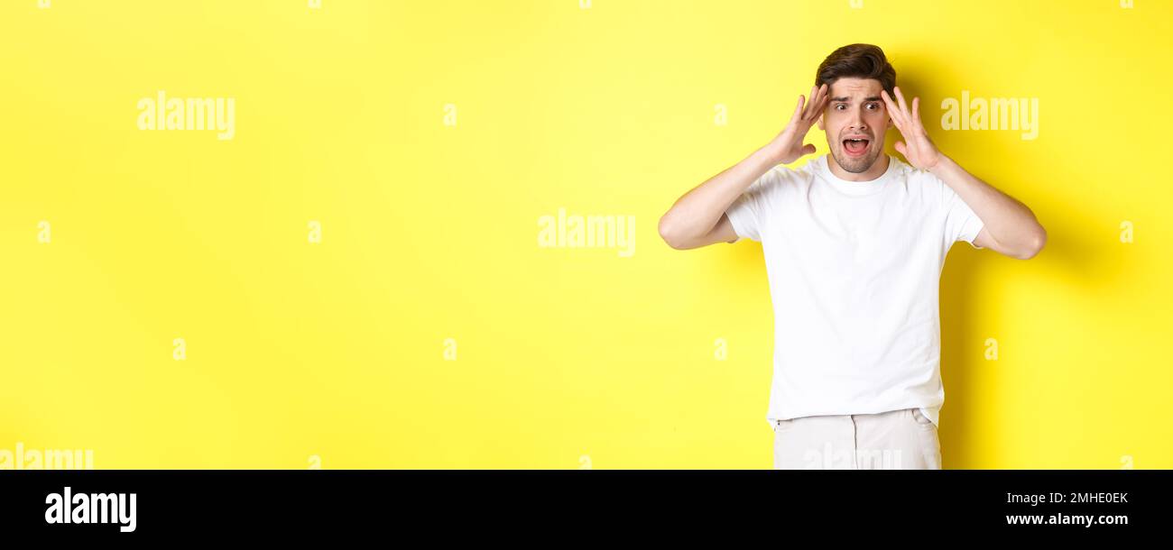 Frustrated guy looking shocked, panicking and holding hands on head ...