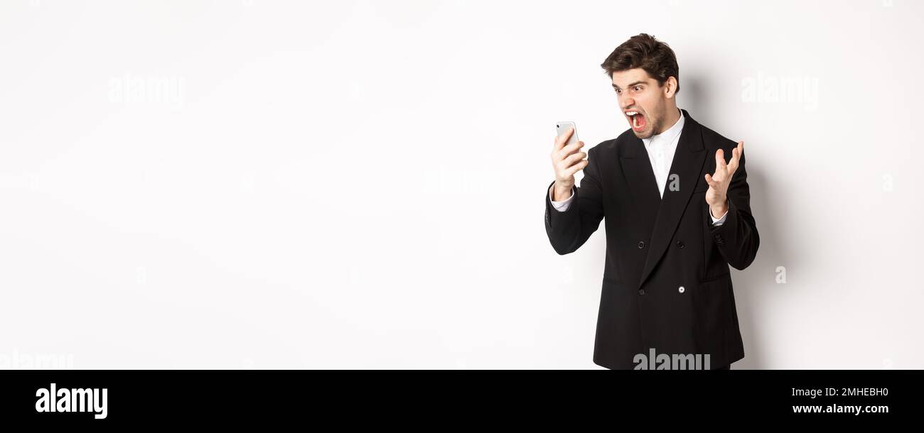 Portrait of angry businessman in black suit yelling at mobile phone ...