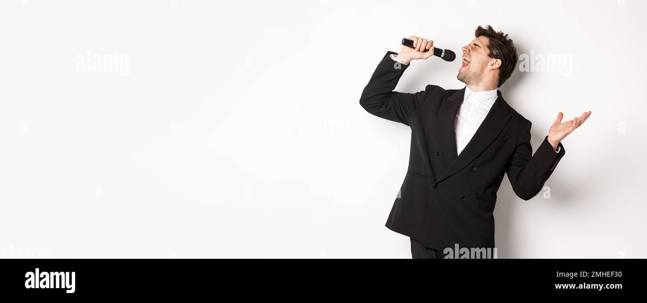 Portrait of handsome man singing a song with passion, standing in black ...