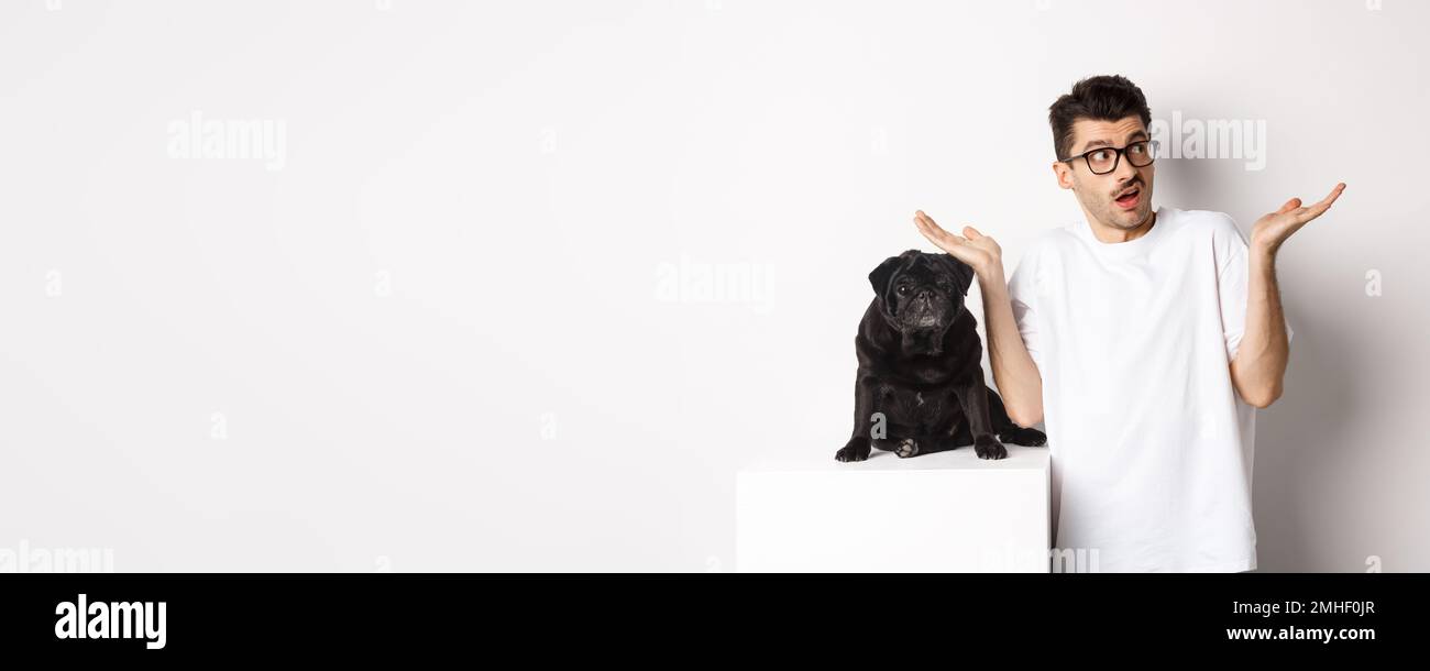 Portrait of confused hipster guy dog owner shrugging, standing near ...