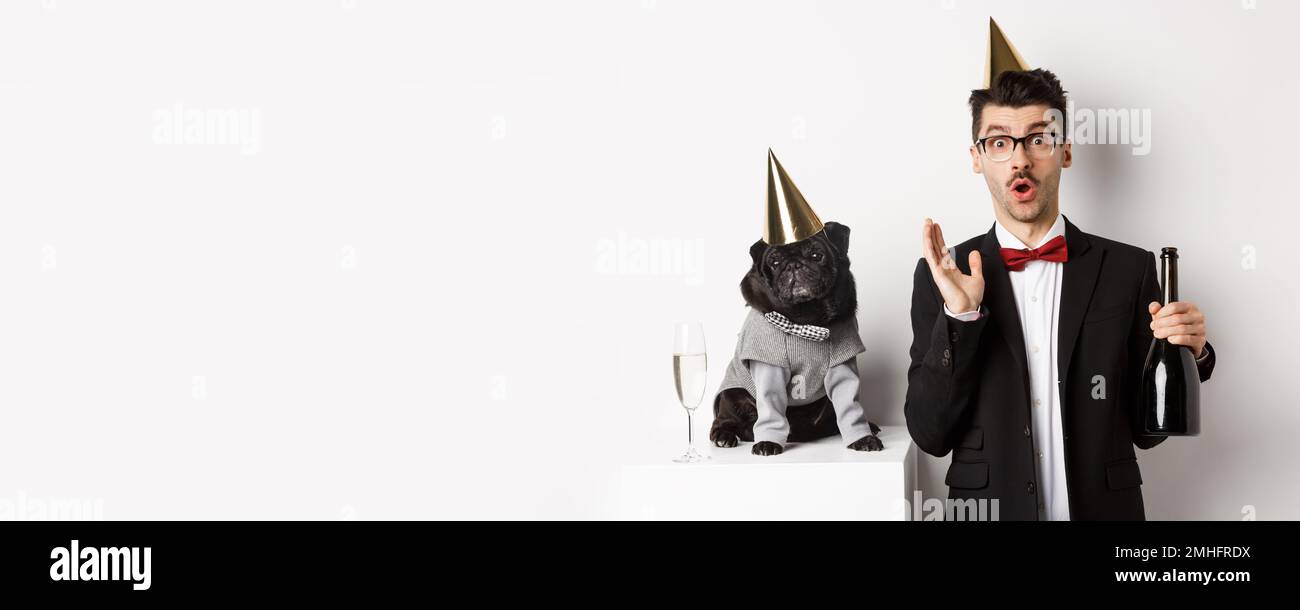 Happy young man celebrating holiday with cute dog, holding champagne ...