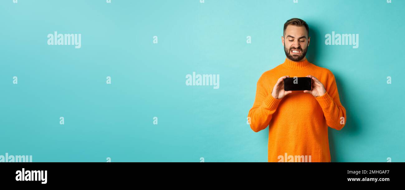 Image of man cringe at something on mobile screen, staring disgusted at ...