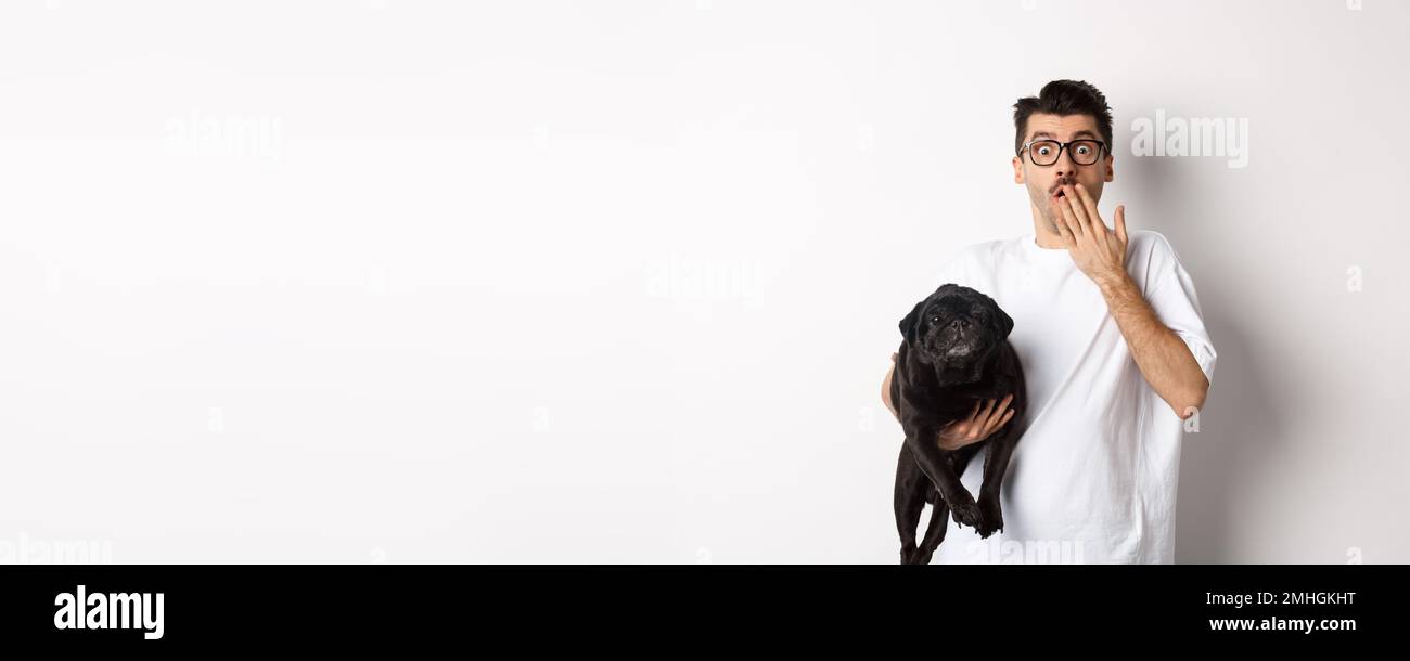 Image of handsome young man holding cute dog and gasping surprised. Pet ...