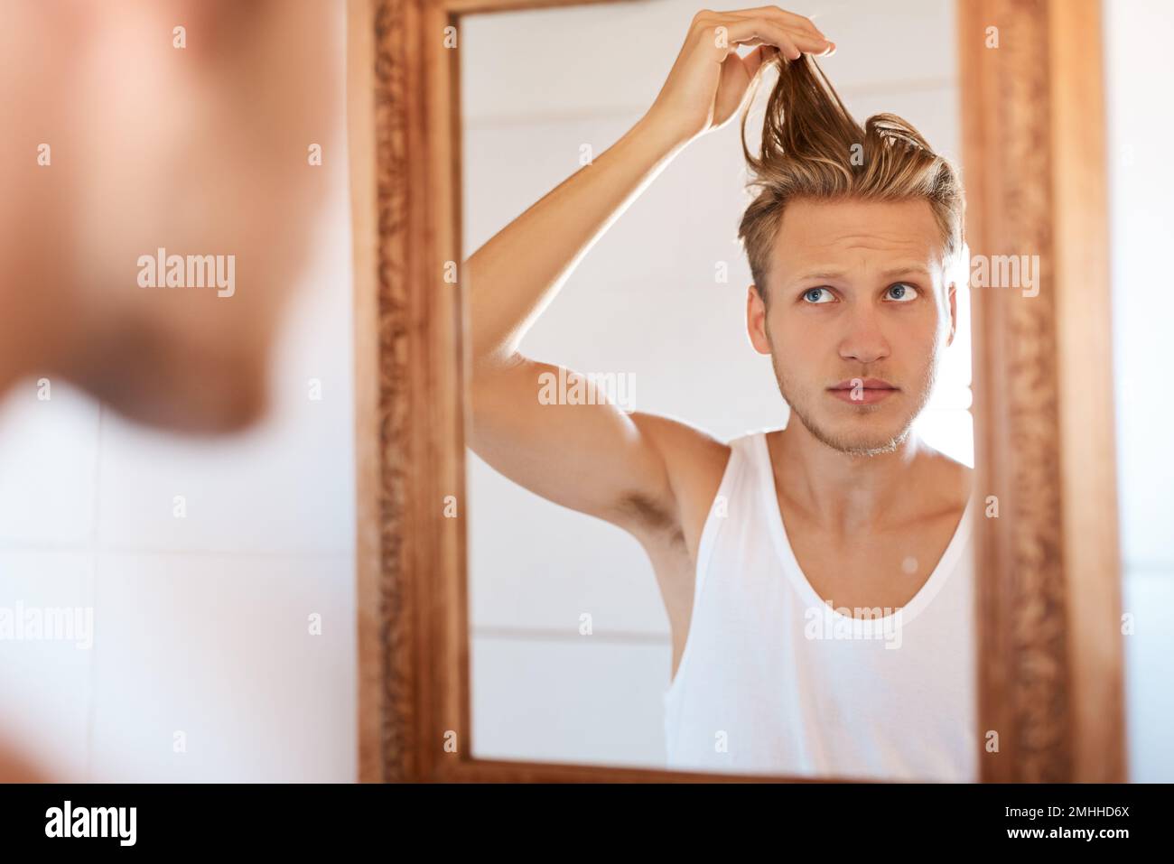 Tired of the same, boring hairstyle. a young man looking at his hair in ...