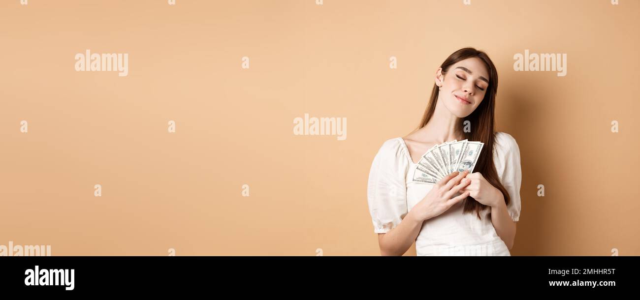 Stylish girl hugging money with pleased smile and closed eyes, like ...