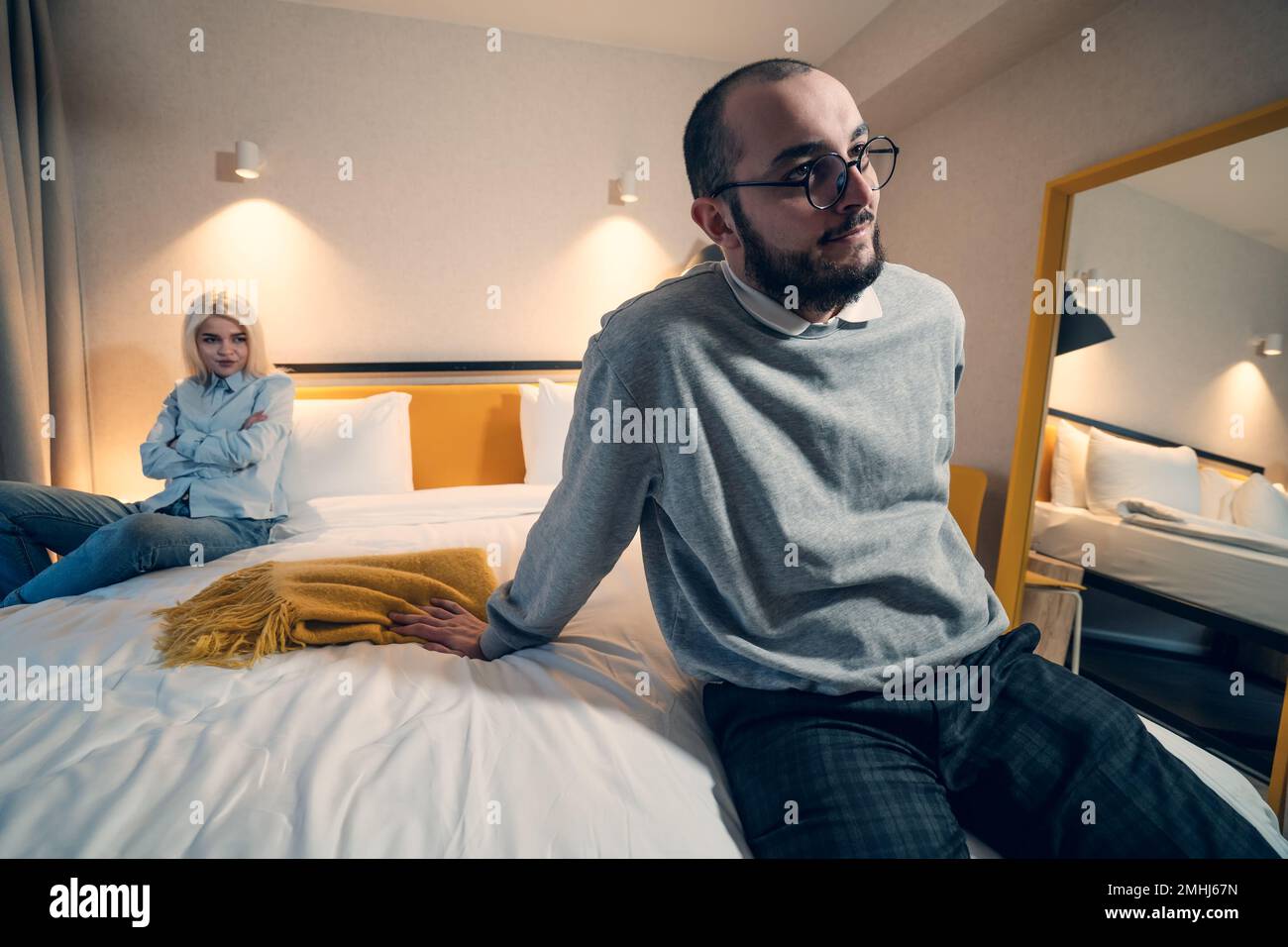 Worried man sit on bed in bedroom, his angry wife looks at him Stock ...