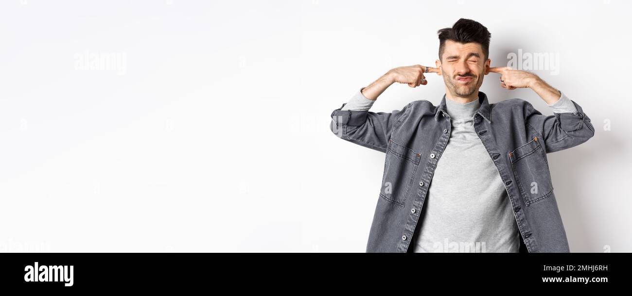Annoyed young man plug ears with fingers and grimacing from loud noise ...