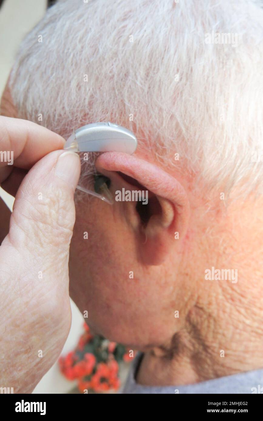 An assistant helps an elderly gentleman put his hearing instrument to ...