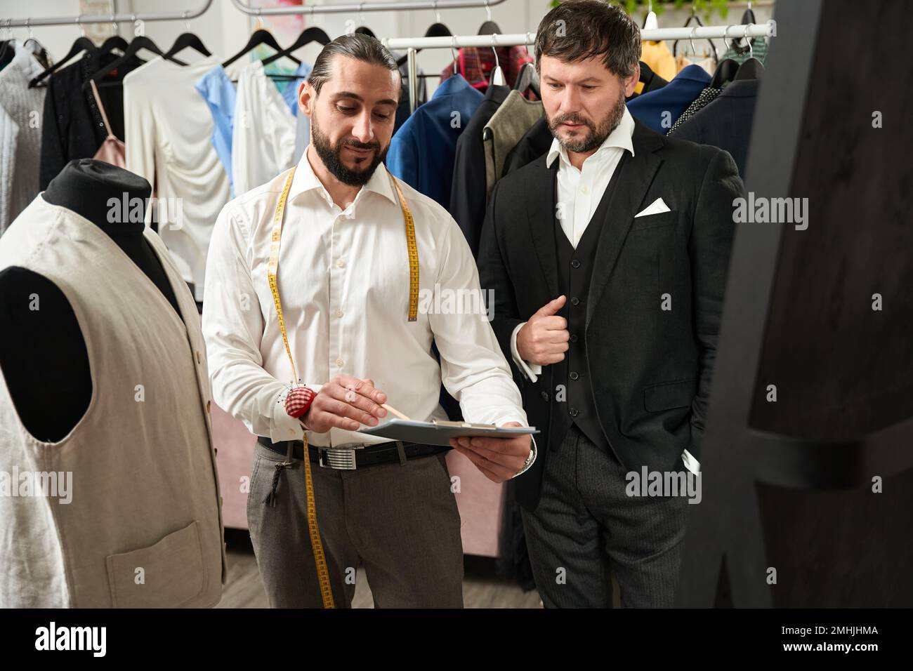 Pleased fashion designer showing client sketch of new suit Stock Photo ...