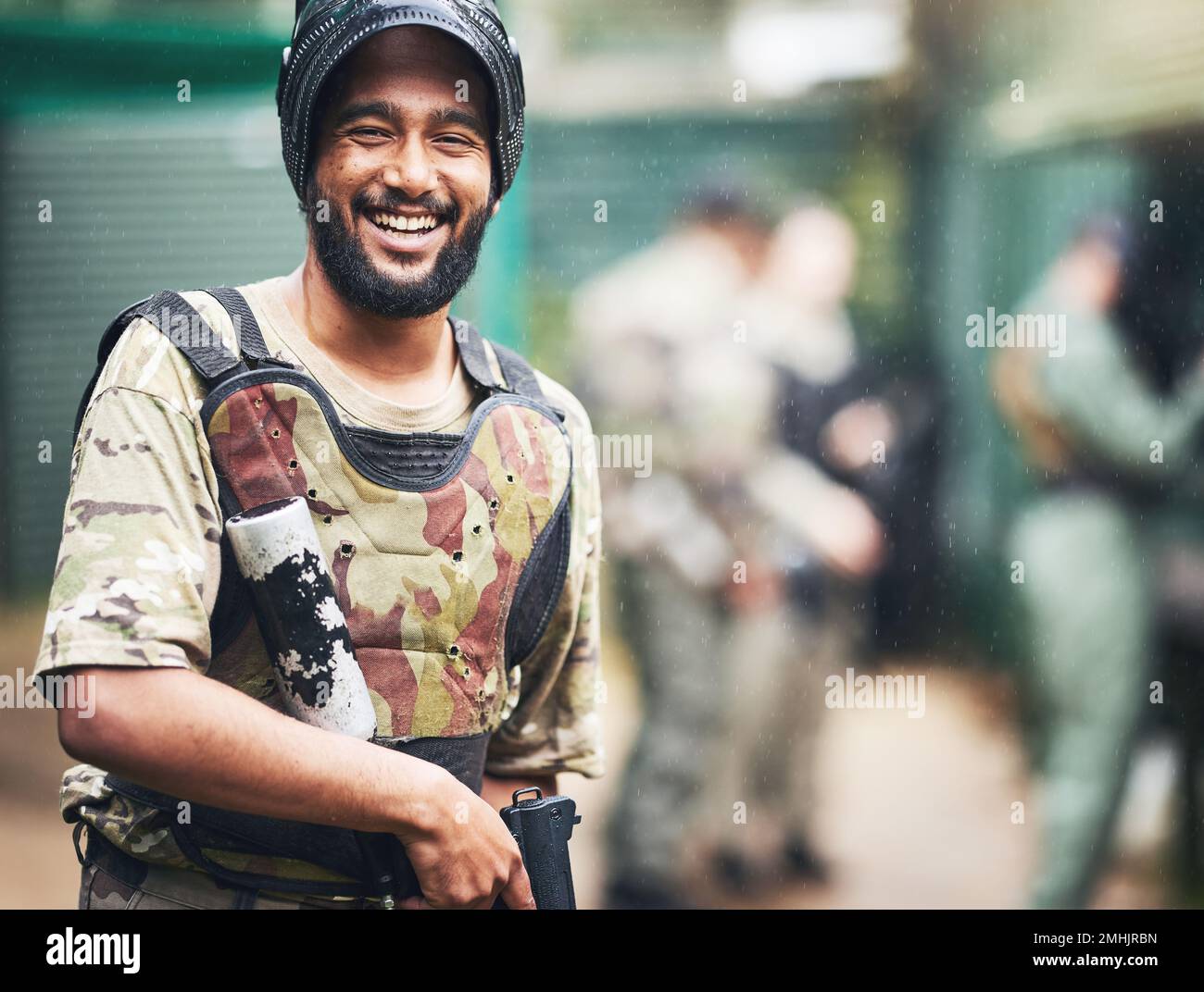 Happy, portrait or man with paintball gun in games arena, team ...