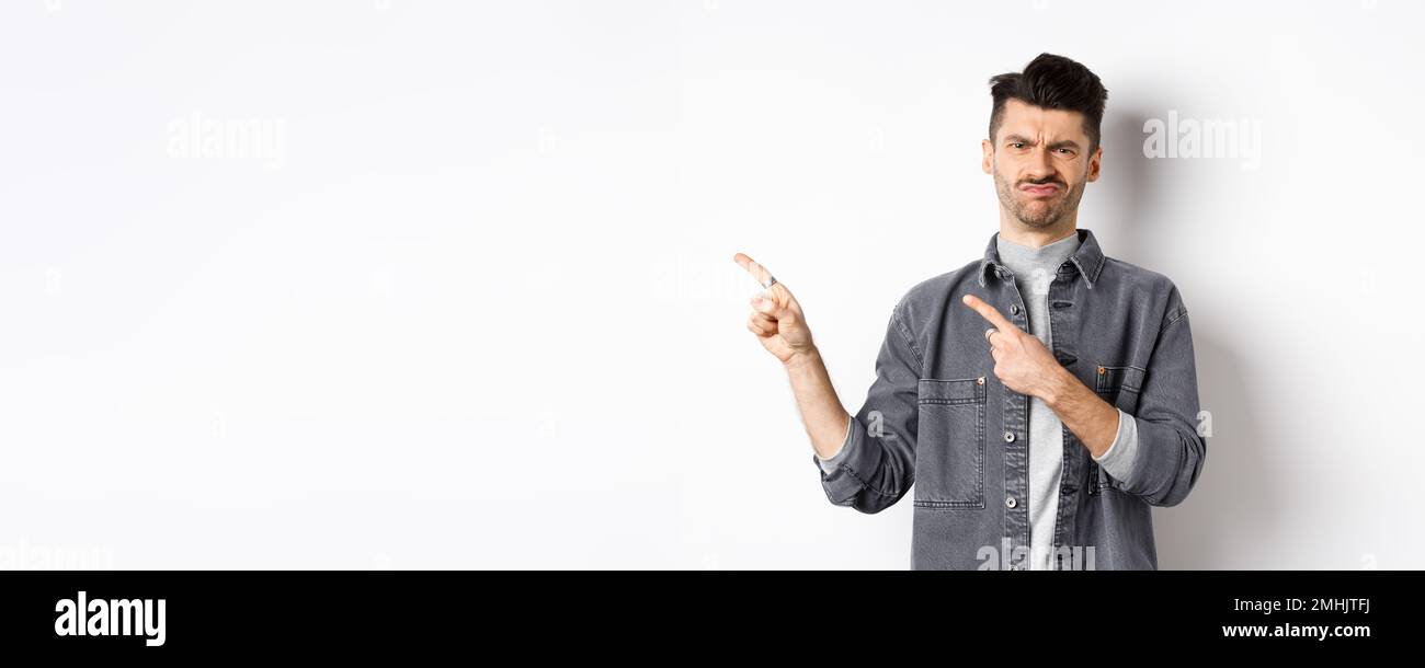 Skeptical and disappointed young man pointing fingers left, grimacing ...
