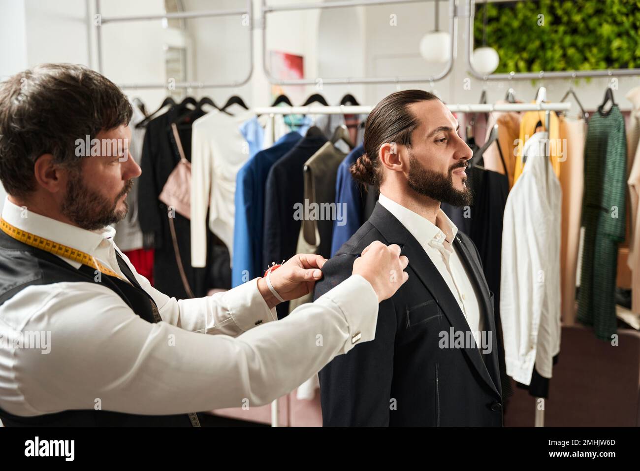 Experienced tailor fastening part of garment on client with pins Stock ...