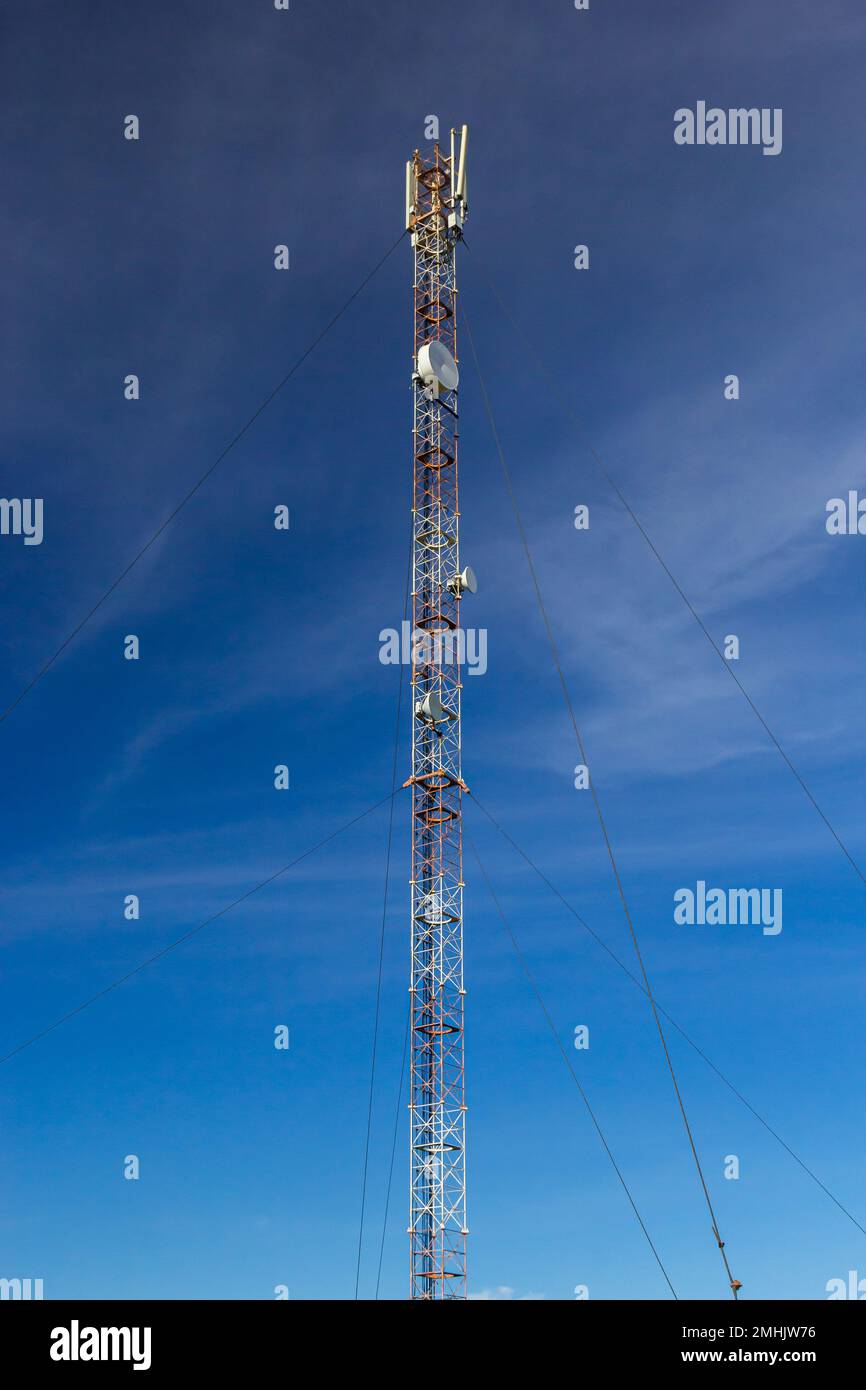Telecommunication tower for mobile phone with antennas over a blue sky. Distribution function of ...