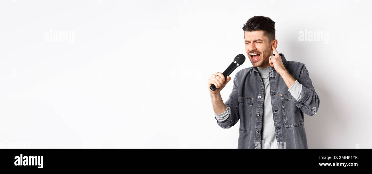 Handsome singer trying to reach high note, singing in microphone and ...